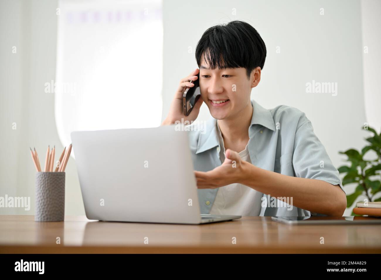 Handsome young Asian man on the phone with his coworker, explaining ...