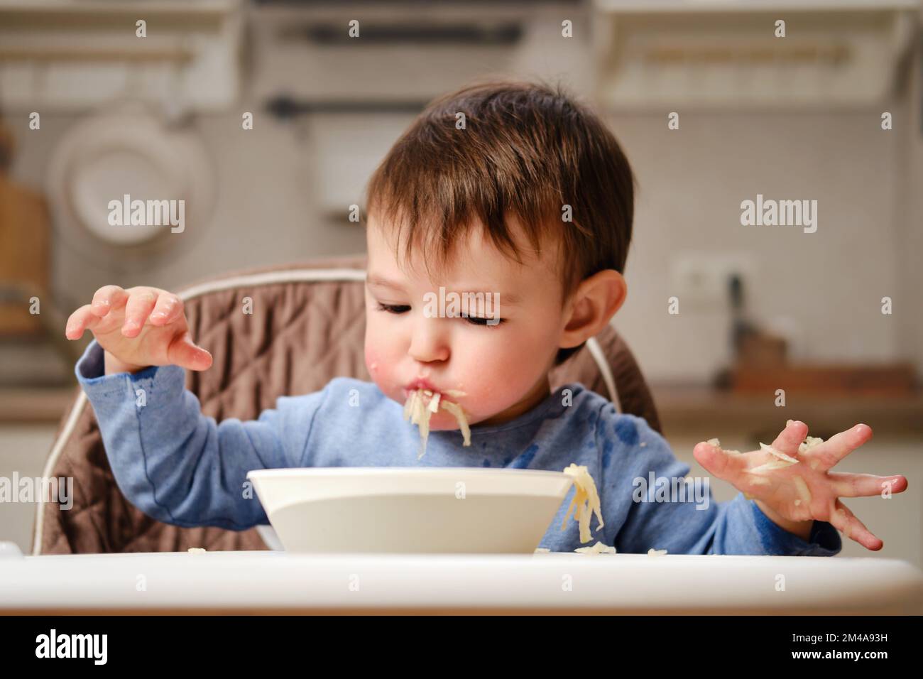 A funny child is eating a grated apple with his mouth full while ...