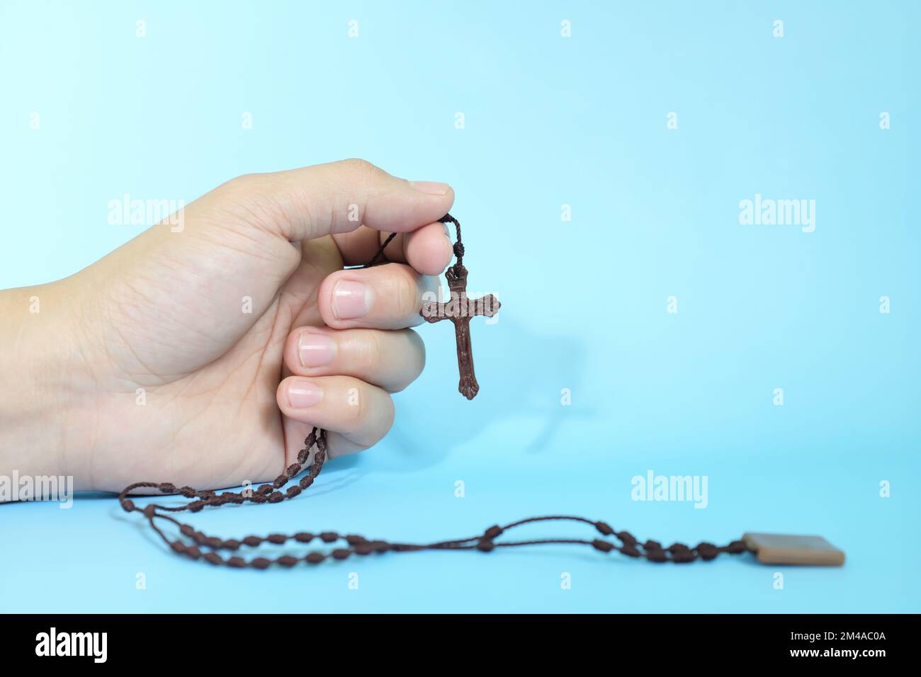 Human hand praying and holding a scapular rosary in blue background ...