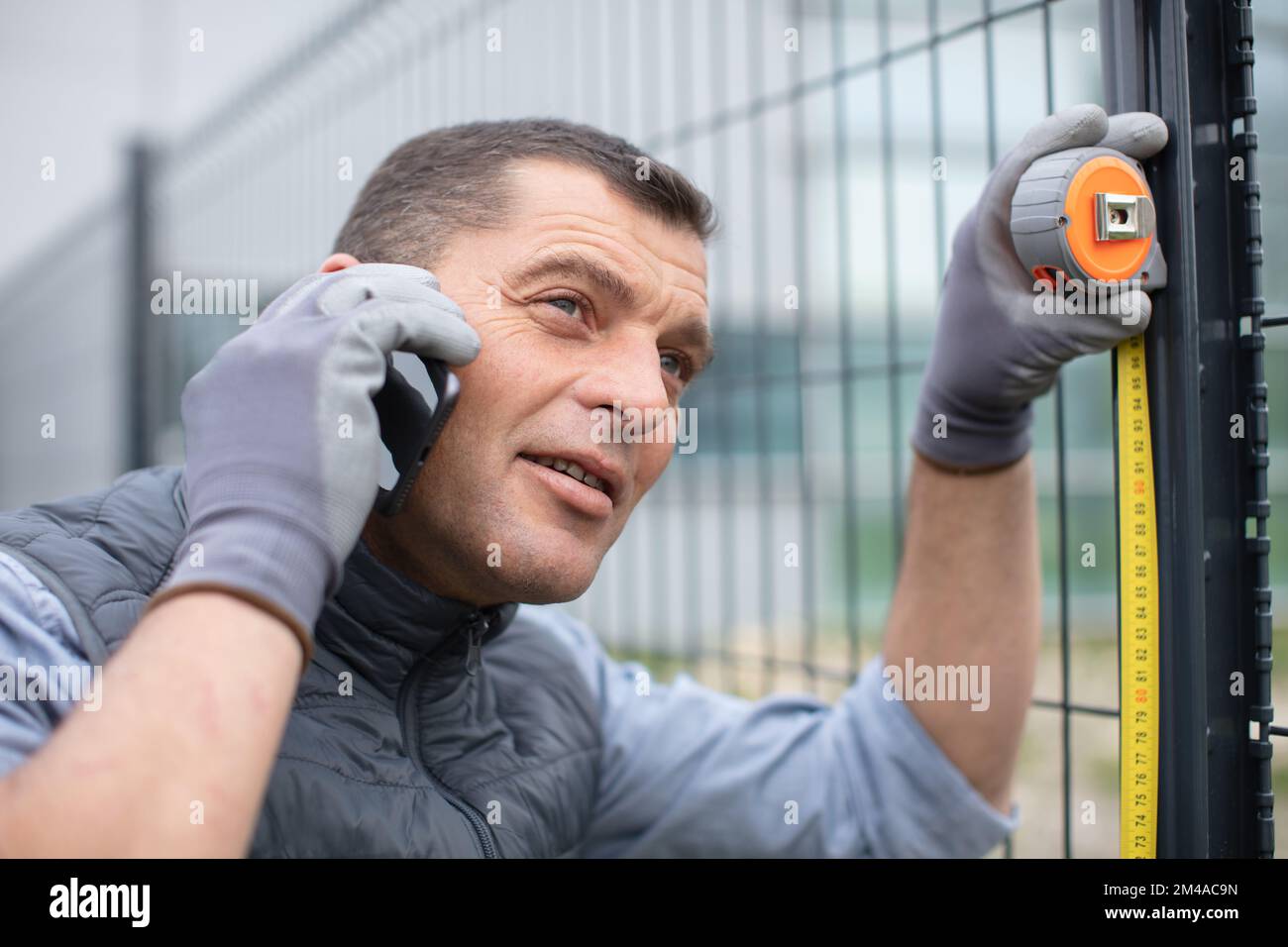 handy man measuring metal fence while calling on phone Stock Photo - Alamy