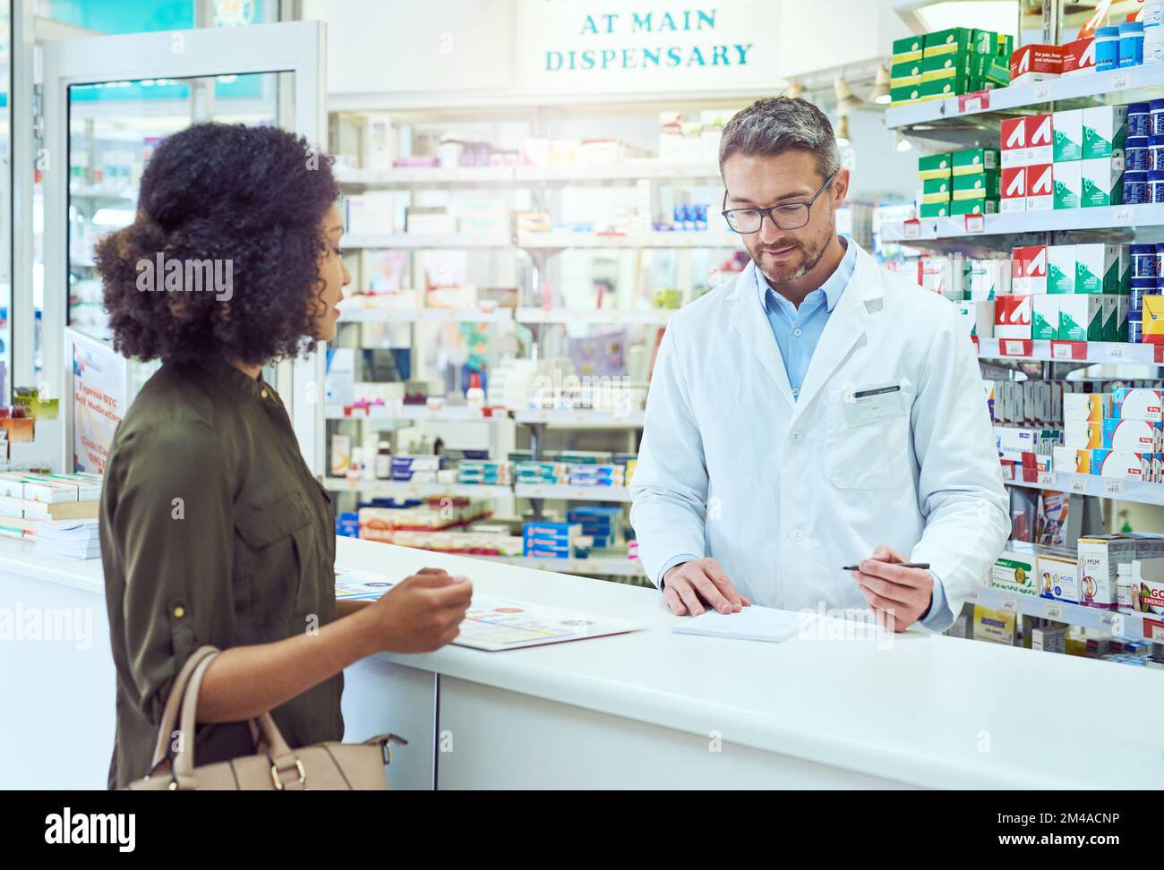 Filling out her prescription. a handsome mature male pharmacist helping ...