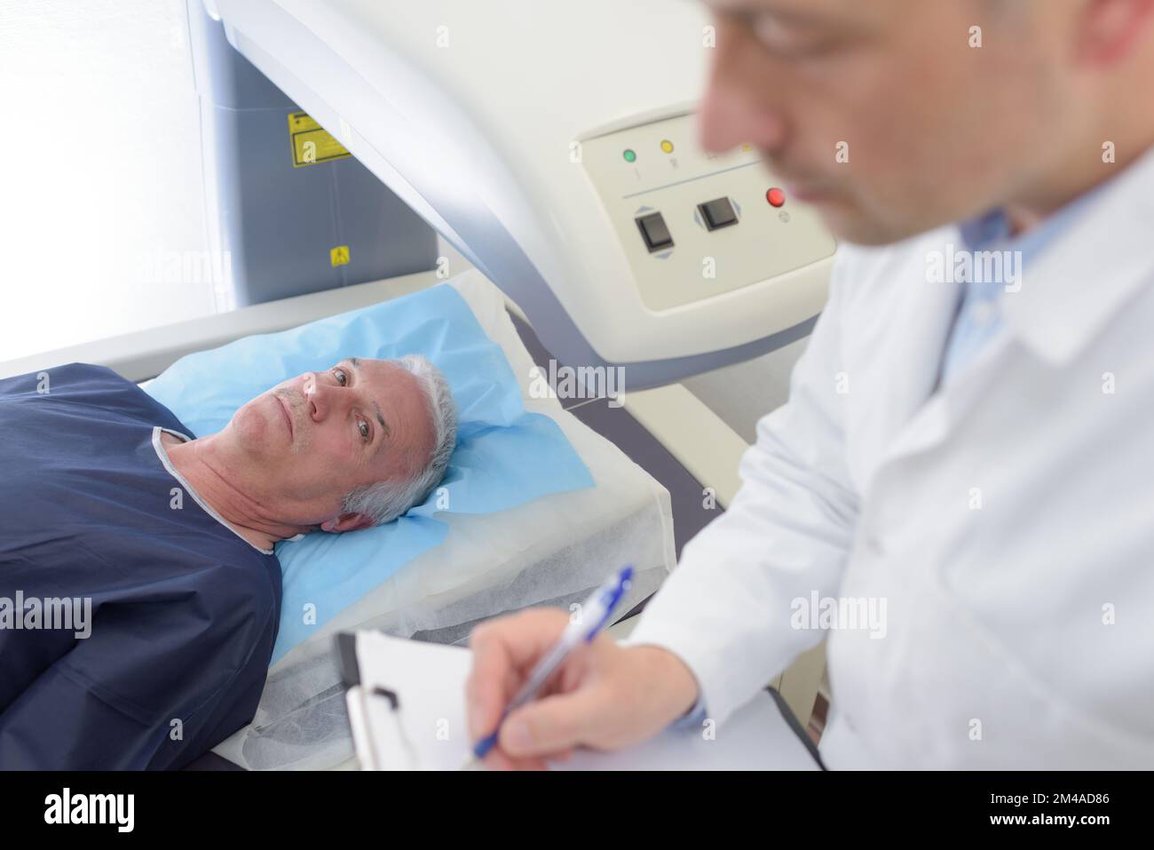 doctor making notes as patient lays under scanner Stock Photo - Alamy