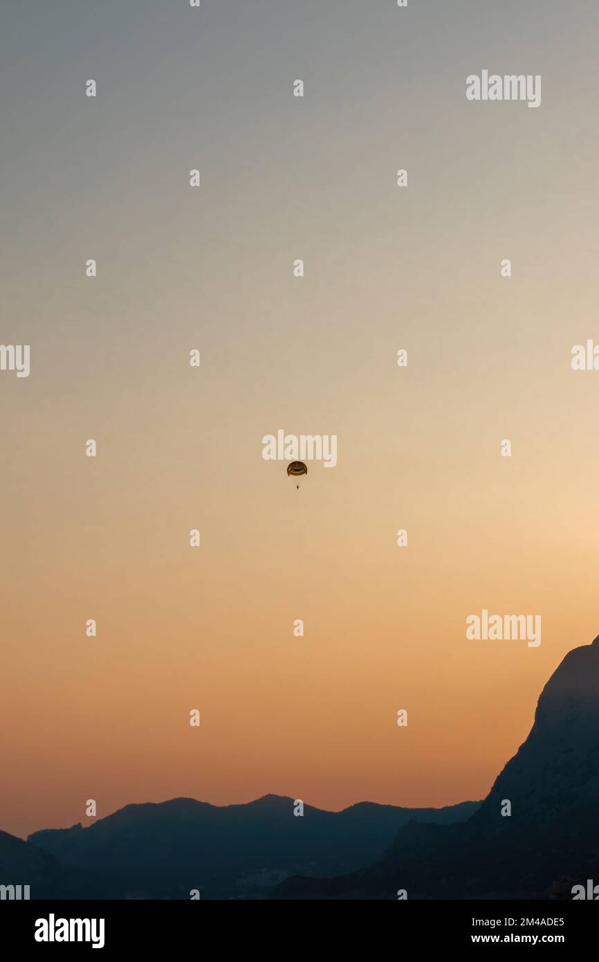 Silhouette of a paraglider soaring over the mountains and the sea at sunset. Extreme sports ...