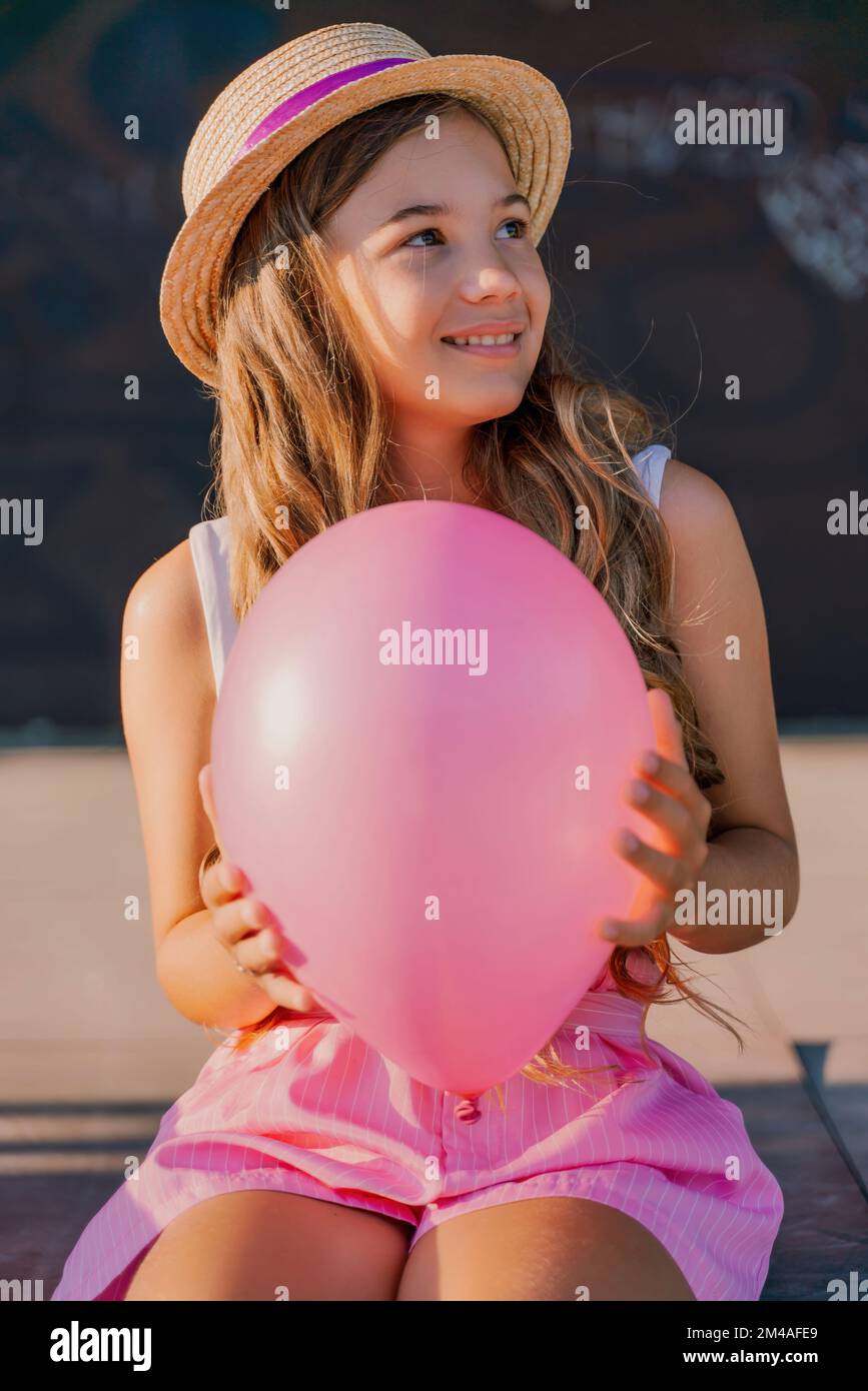 Portrait of a girl in a hat with a pink balloon. She is dressed in pink ...