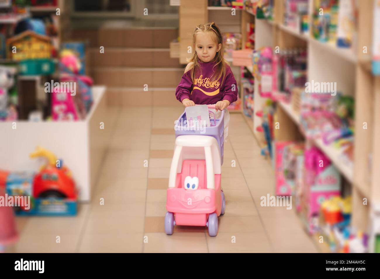 Little girl with small shopping cart in kids mall. Happy girl choosing ...