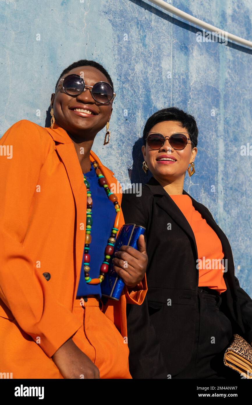 From below positive stylish multiracial female friends in classy suits ...