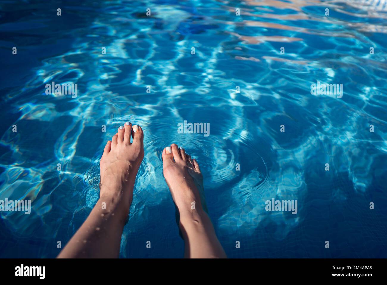 From above anonymous barefoot female tourist wetting legs in blue water ...