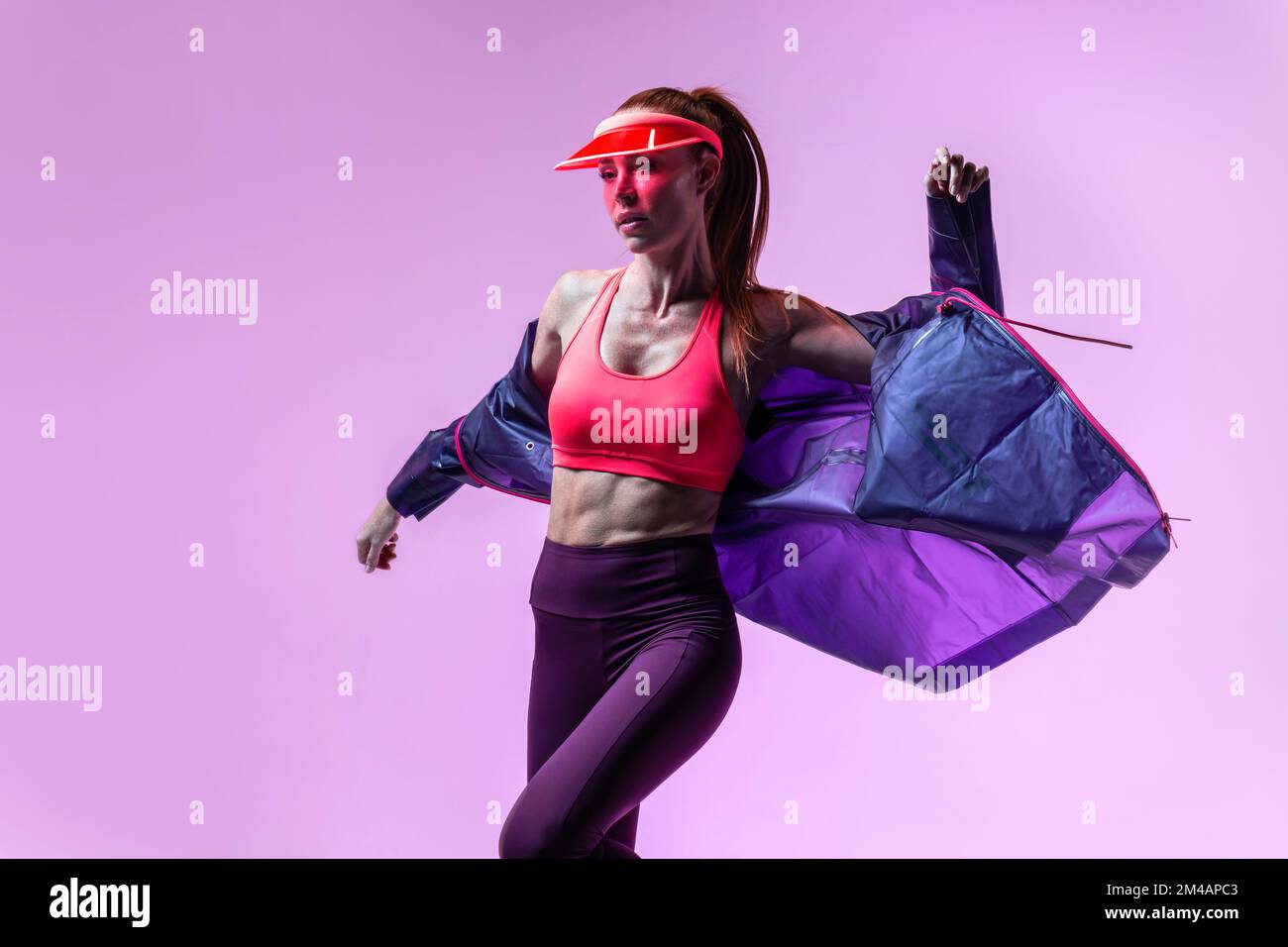Slim female athlete in stylish sportswear with raincoat and cap ...
