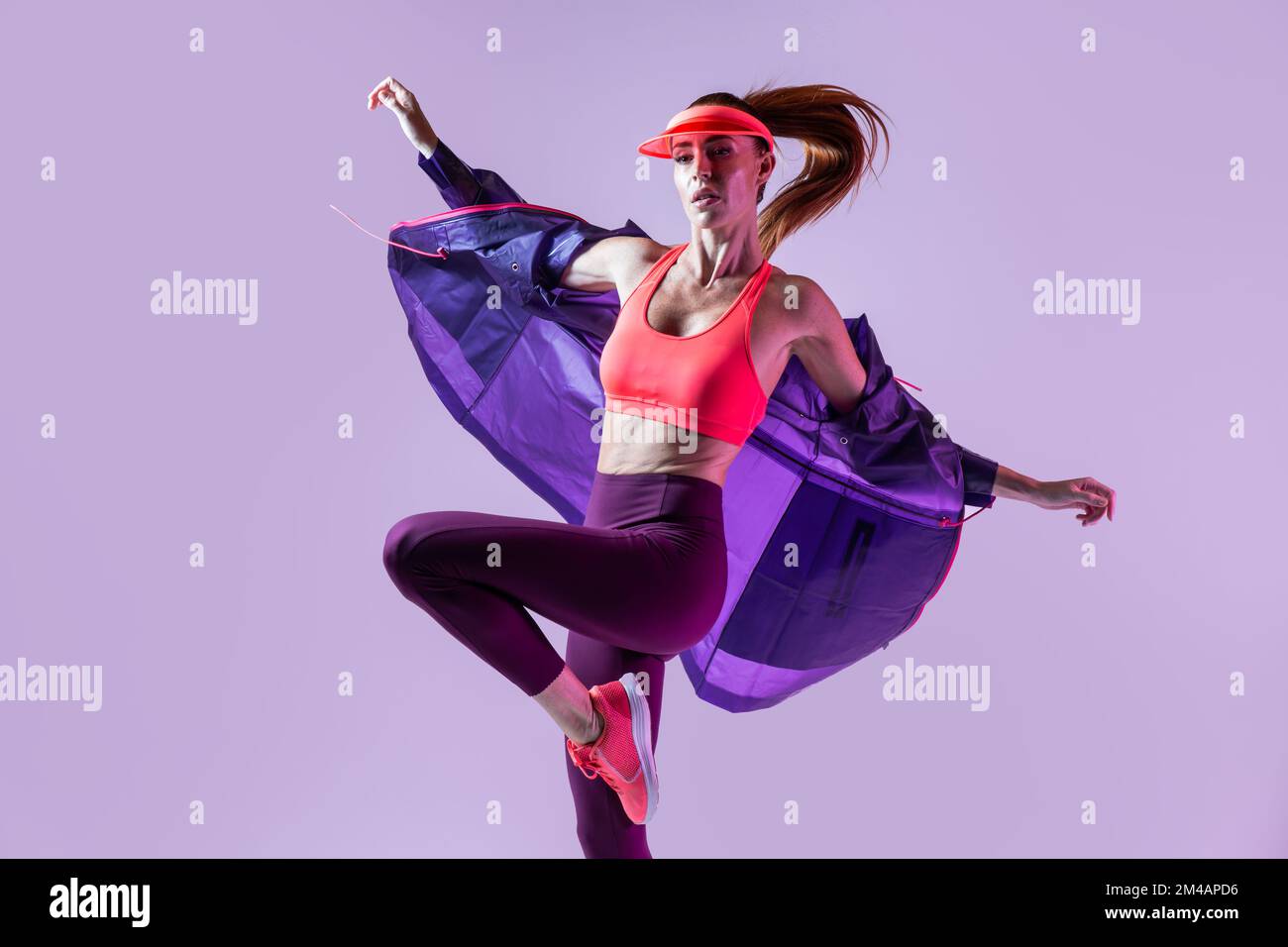 Slim female athlete in stylish sportswear with raincoat and cap ...
