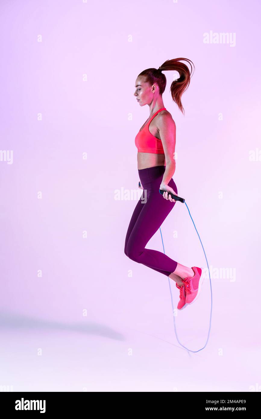 Side view of fit female athlete with ponytail jumping with rope during ...