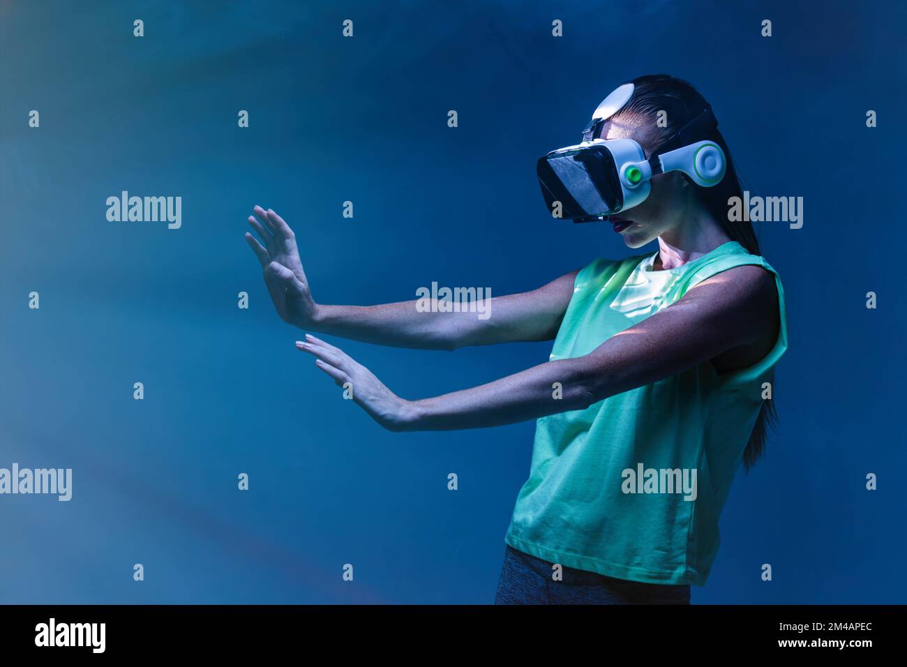 Young female in sportswear in VR headset playing videogame in dark room ...