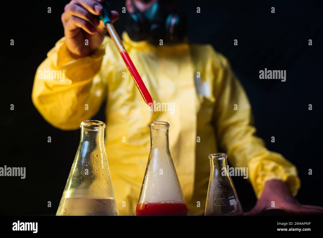 Low angle soft focus man in hazmat suit and gas mask using pipette to ...