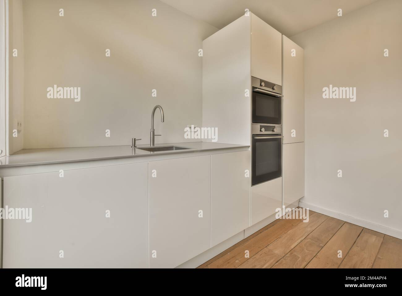 Modern built in ovens installed into white cupboards behind counter in ...