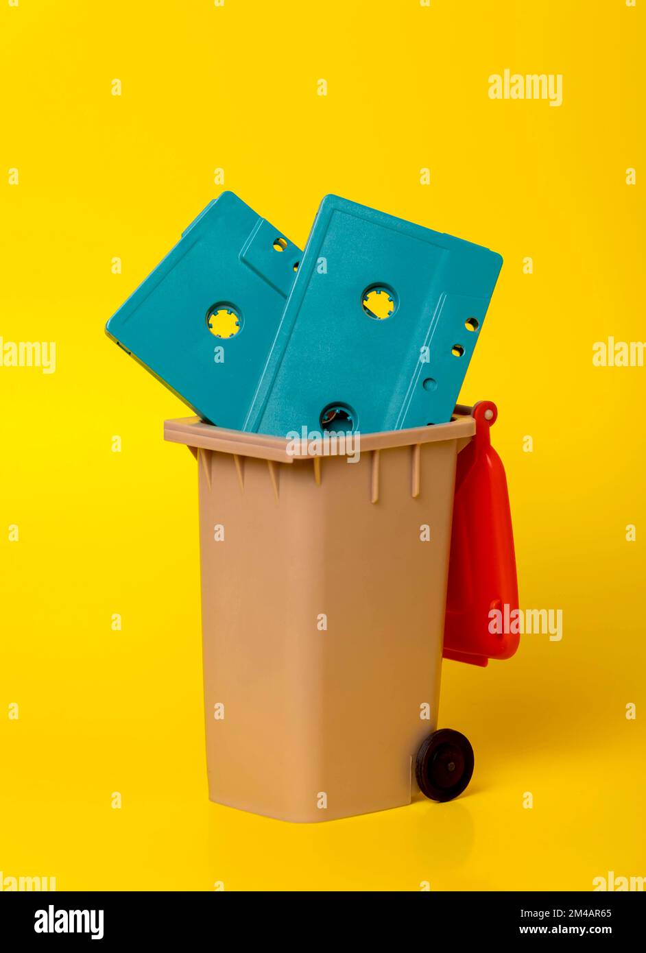 Plastic blue retro tape cassettes in brown waste bin with red lid ...
