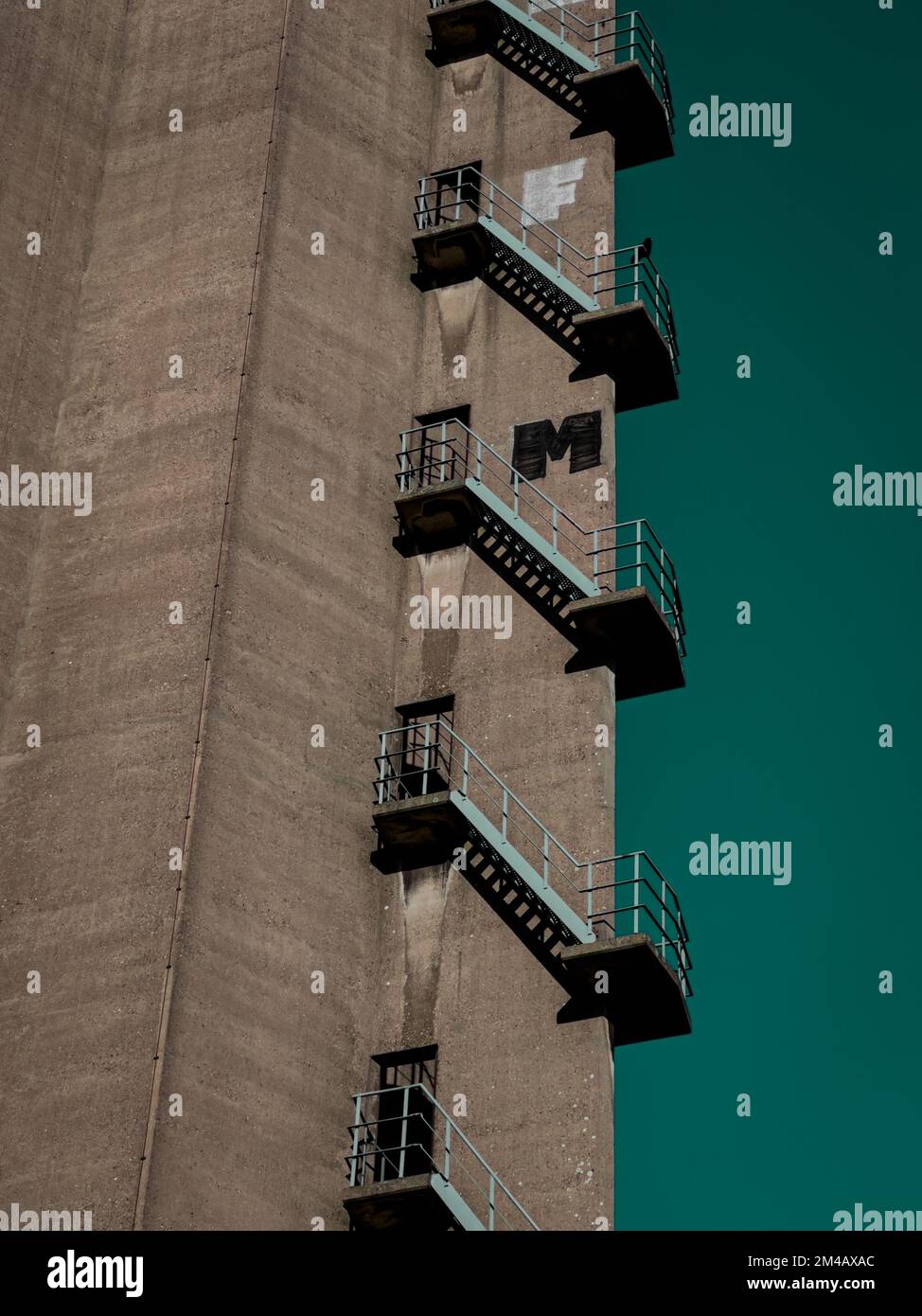 A vertical shot of a tall Industrial building with fire escape stairs ...