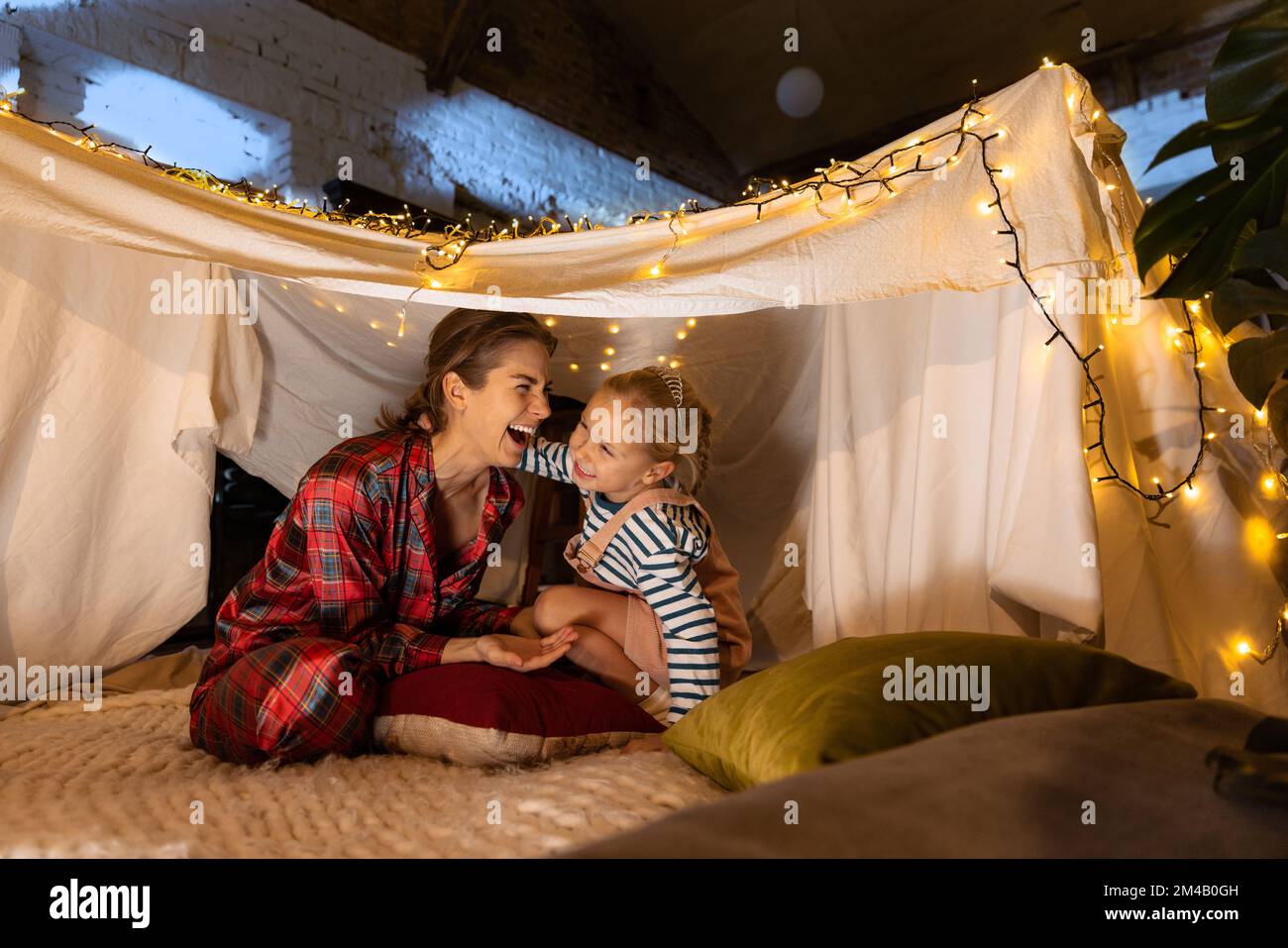 Mother and daughter sitting inside self-made hut, tent in room in the ...