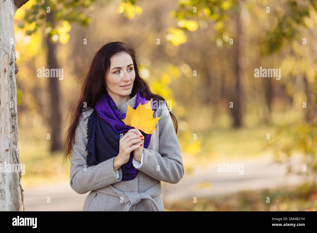 a beautiful girl with dark hair, a wet coat and a purple scarf holds a ...