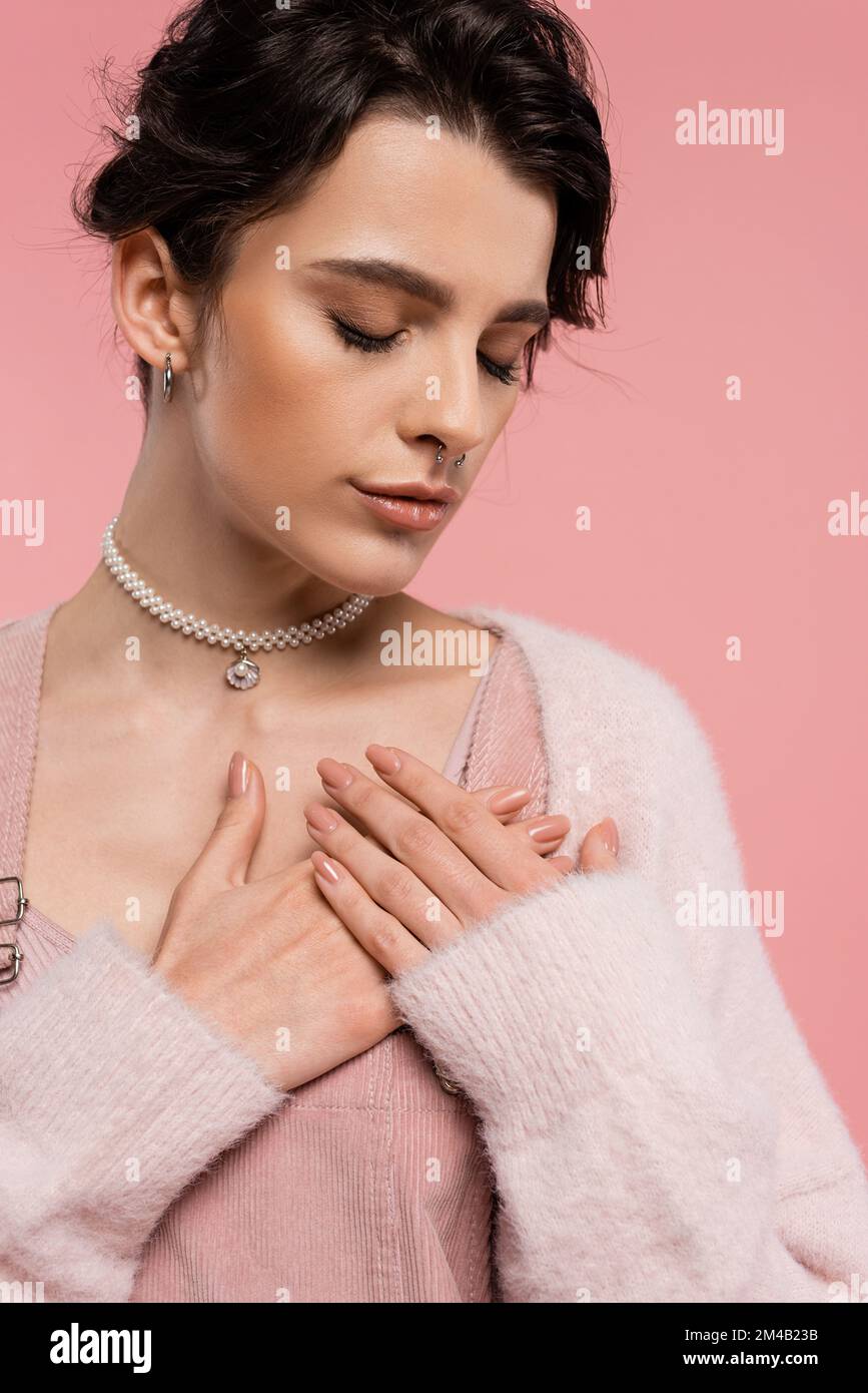 young woman in pearl necklace and piercing posing with hands on chest ...