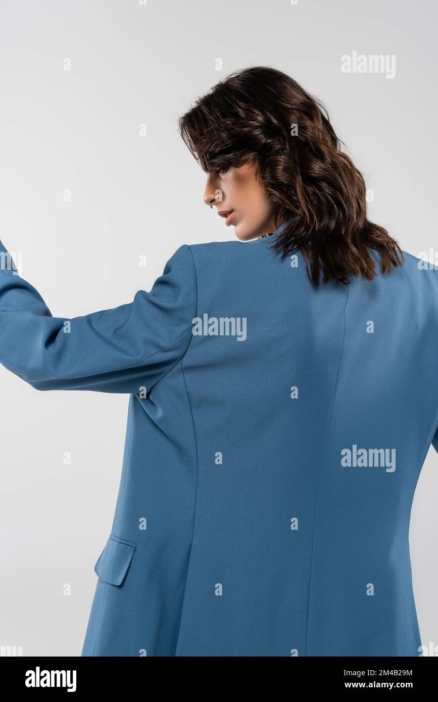 back view of brunette woman in blue blazer posing isolated on grey ...