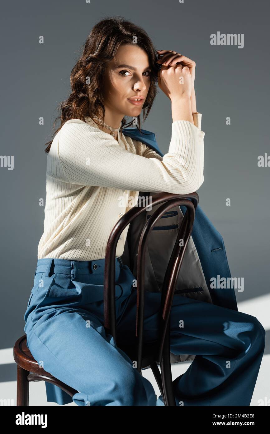 positive woman in white jumper and blue trousers sitting on chair and ...