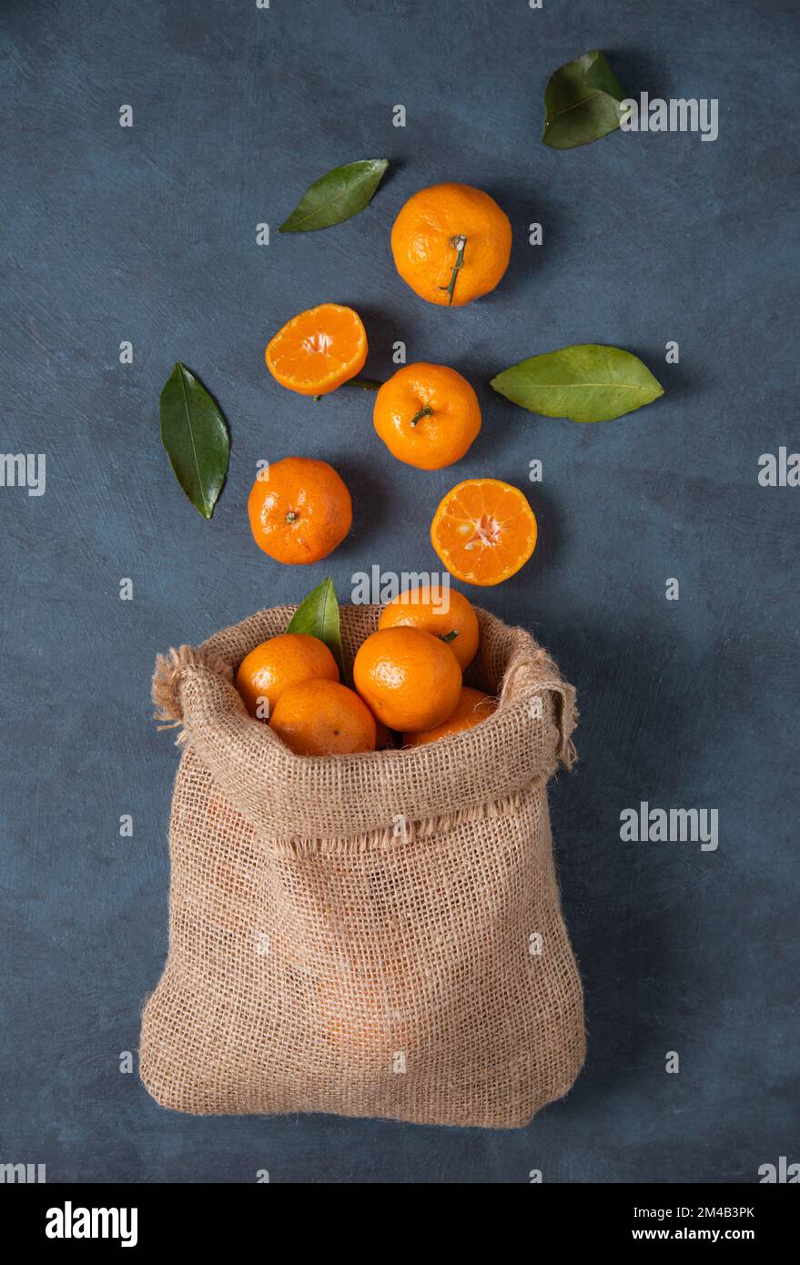 sweet tangerines with green leaves fall out of a crafting bag on a dark ...