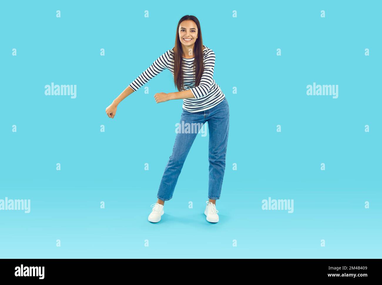 Young woman in casual clothes doing funny floss dancing move on blue ...