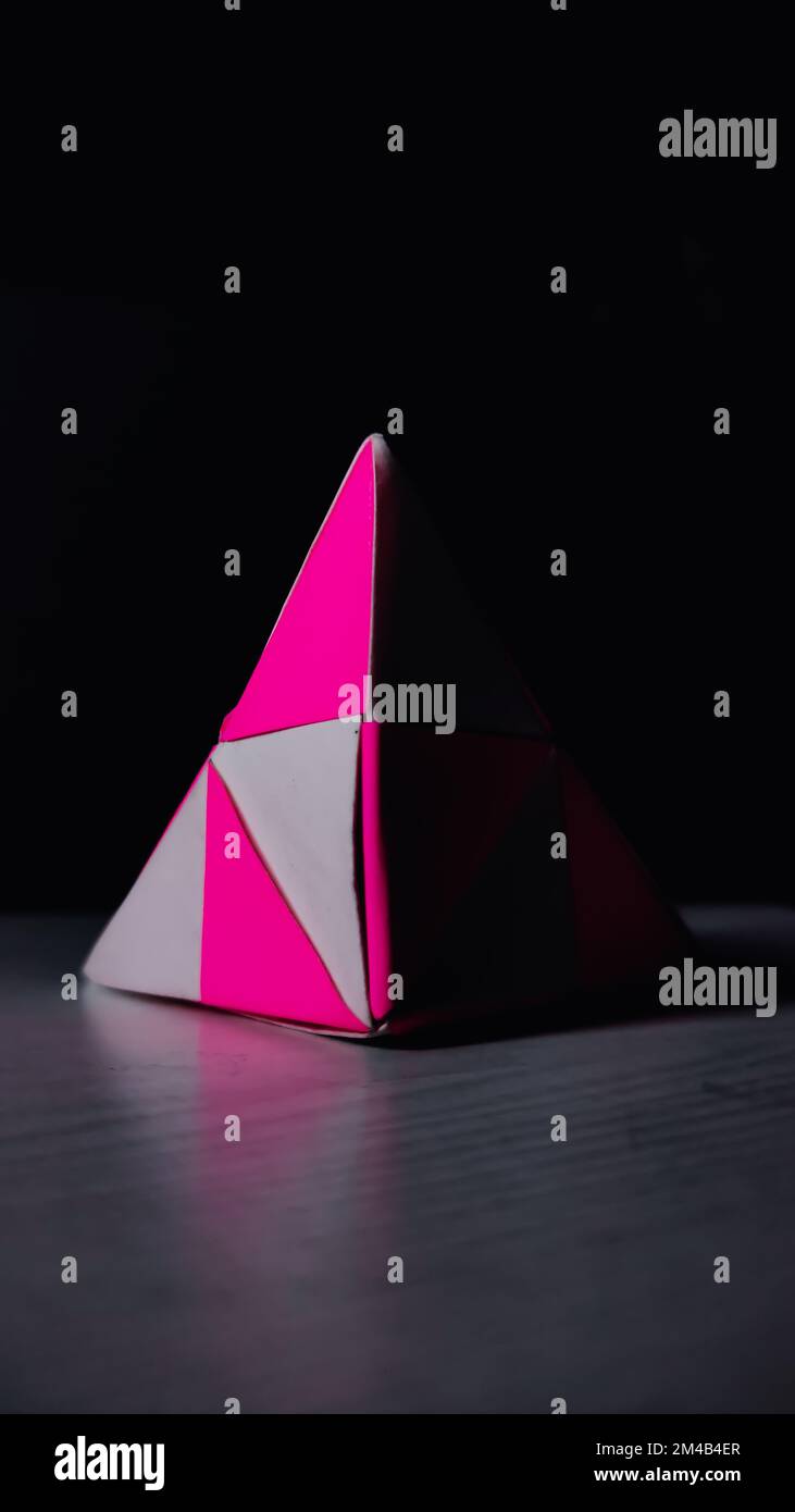 A vertical shot of a pink and white origami pyramid on a black surface ...