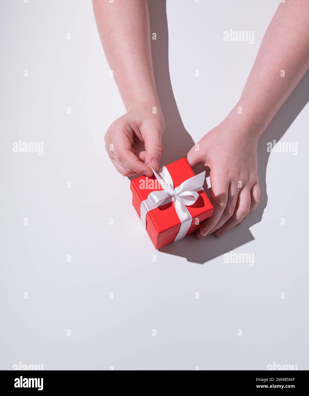 Childrens hands open red holiday gift box with white ribbon. Top view ...