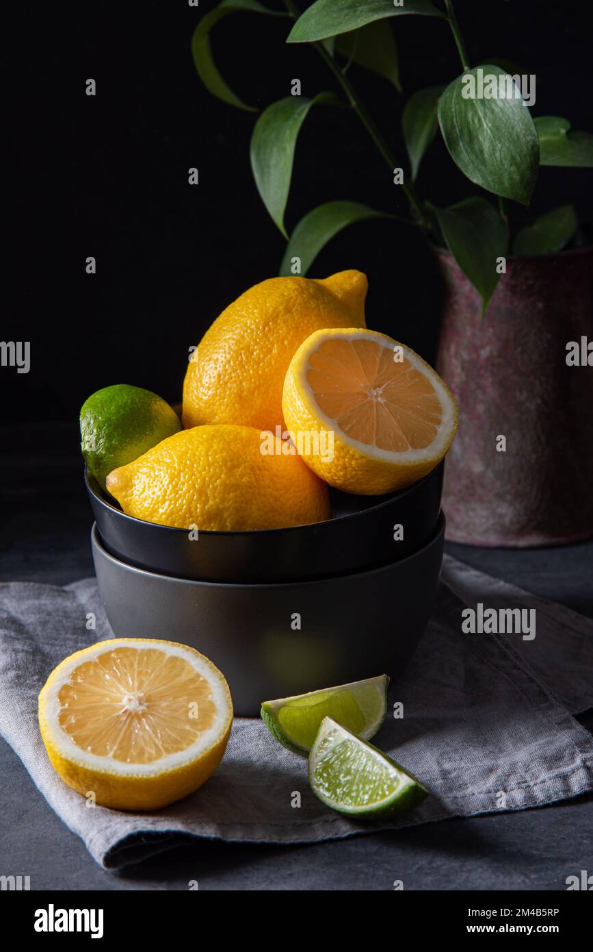 juicy lemons and limes in a black bowl on a gray table. Dark and mood ...
