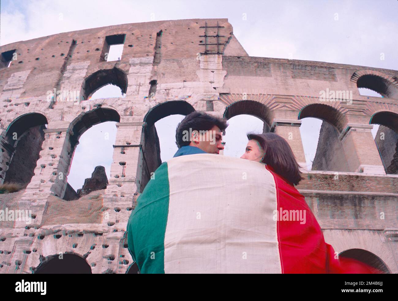 Boy and girl hugging with the Italian flag in front of the Coliseum ...