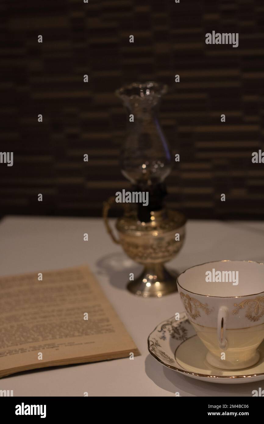 photo of an open book and a kerosene lamp and an empty cup and saucer ...