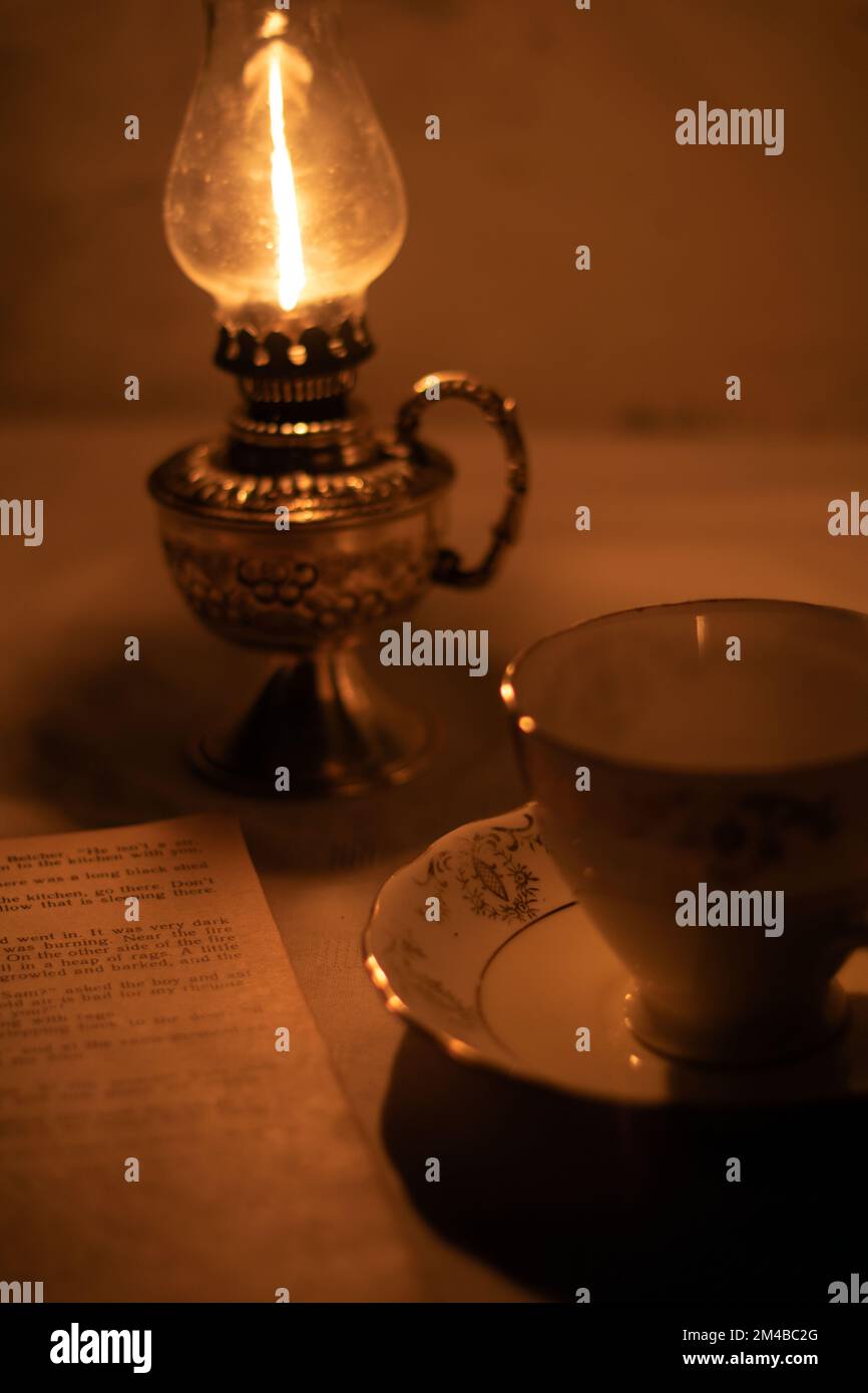 photo of a burning kerosene lamp and an old book with an empty cup on ...
