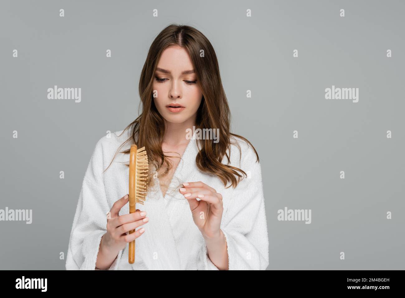 stressed young woman holding wooden hair brush and pulling damaged hair ...
