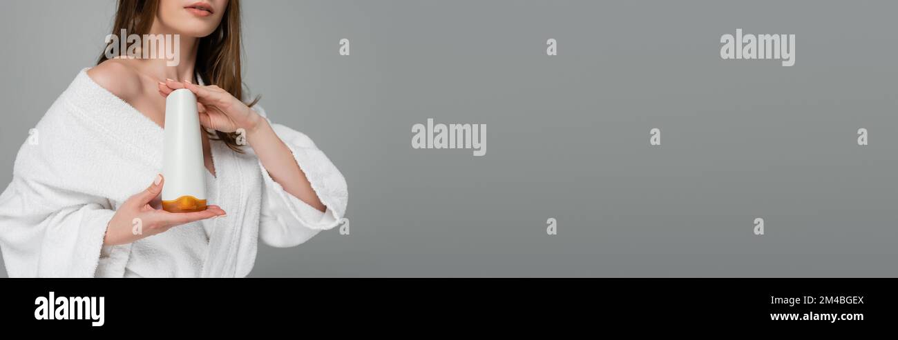 partial view of young woman with shiny hair holding bottle with shampoo ...