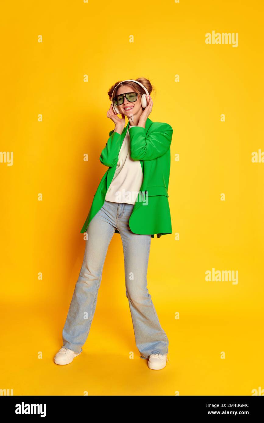 Portrait of young girl in bright green jacket posing in headphones over ...