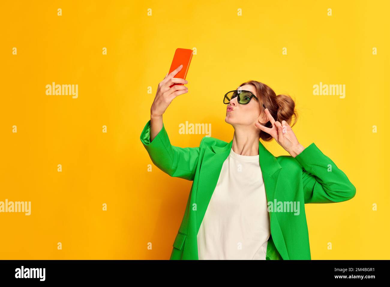 Portrait of young girl in bright green jacket posing, taking selfie ...