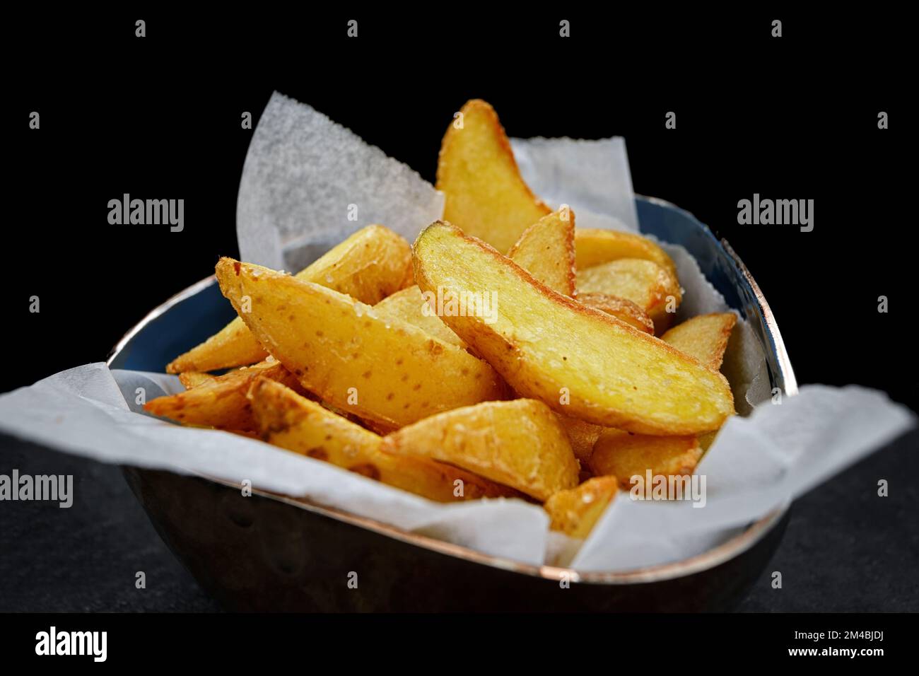 Fried potato wedges on paper, on a black background Stock Photo - Alamy