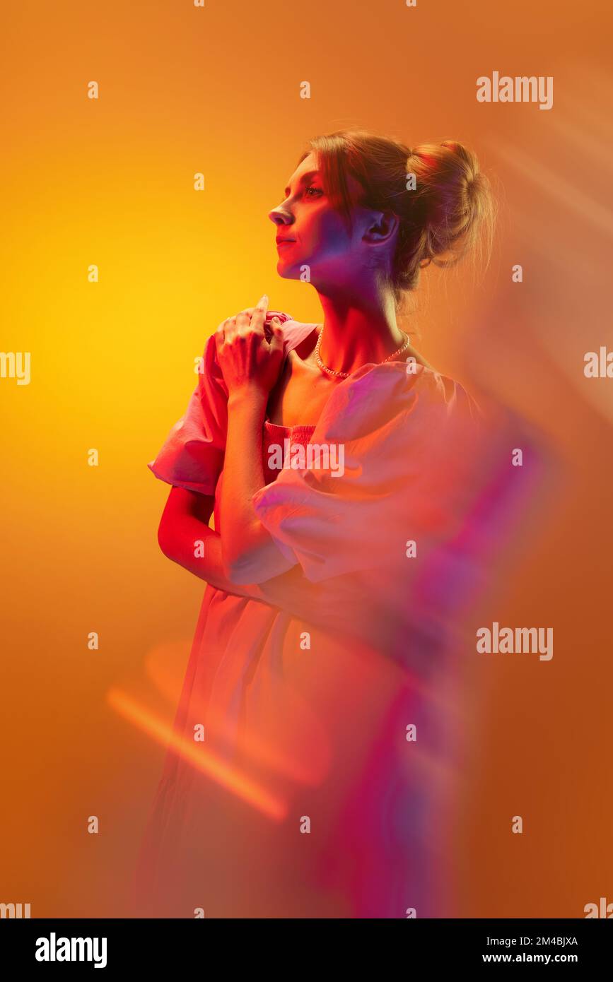 Portrait of young beautiful girl in white dress posing over orange ...