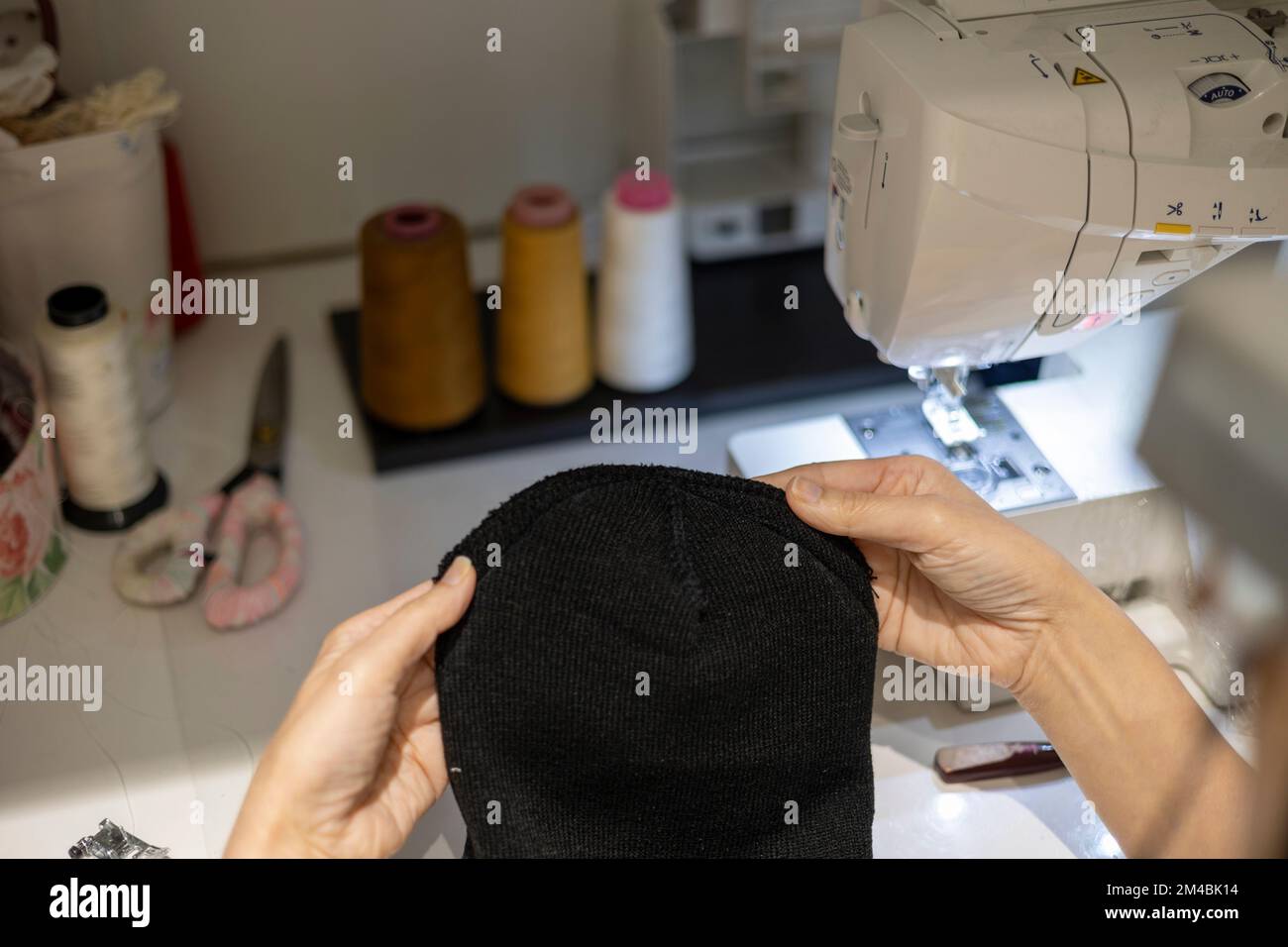 Woman is sewing black beanie hat on a sewing machine, using a sewing ...