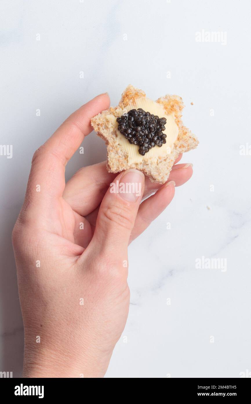 Black caviar appetizers bread stars with butter in a human hand on a ...