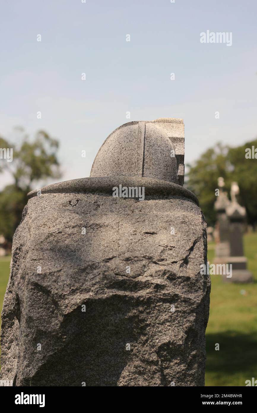 A tombstone standing in the graveyard with a fireman's helmet resting ...