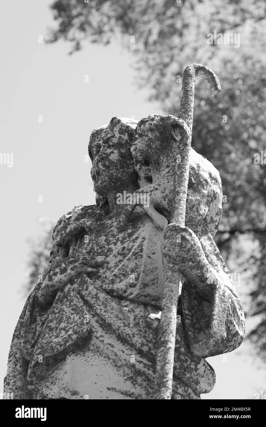 A worn and weathered stone statue of Jesus Christ carrying a lamb on ...