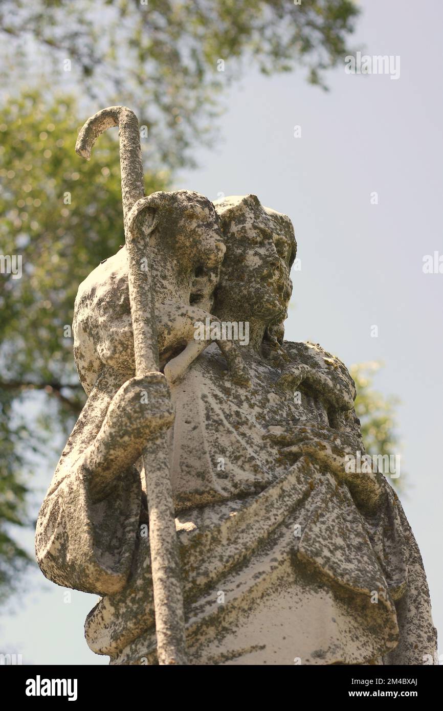 A worn and weathered stone statue of Jesus Christ carrying a lamb on ...