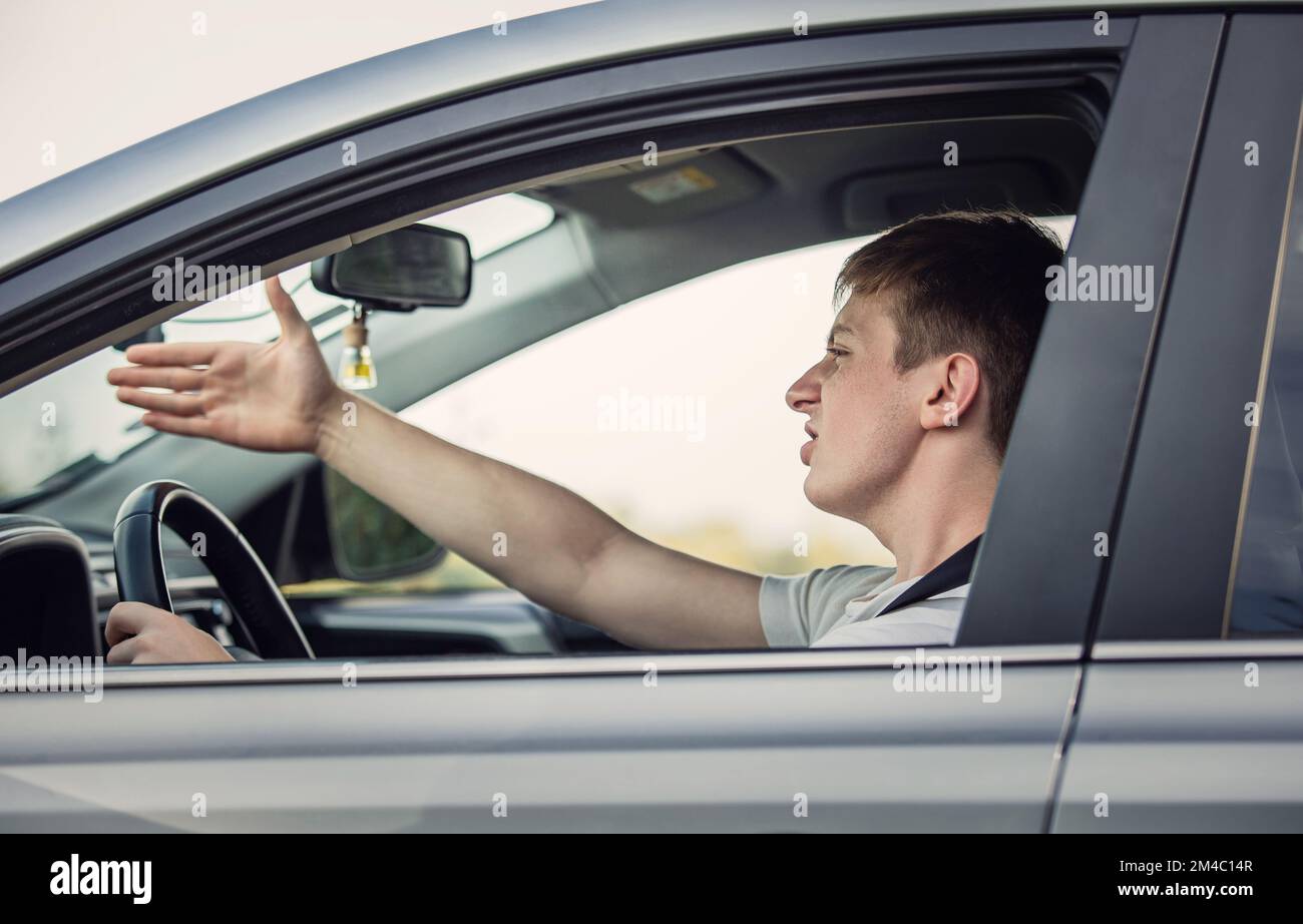 Furious driver gesturing with his hand to the traffic jam ahead his car. Aggressive guy unsafe ...