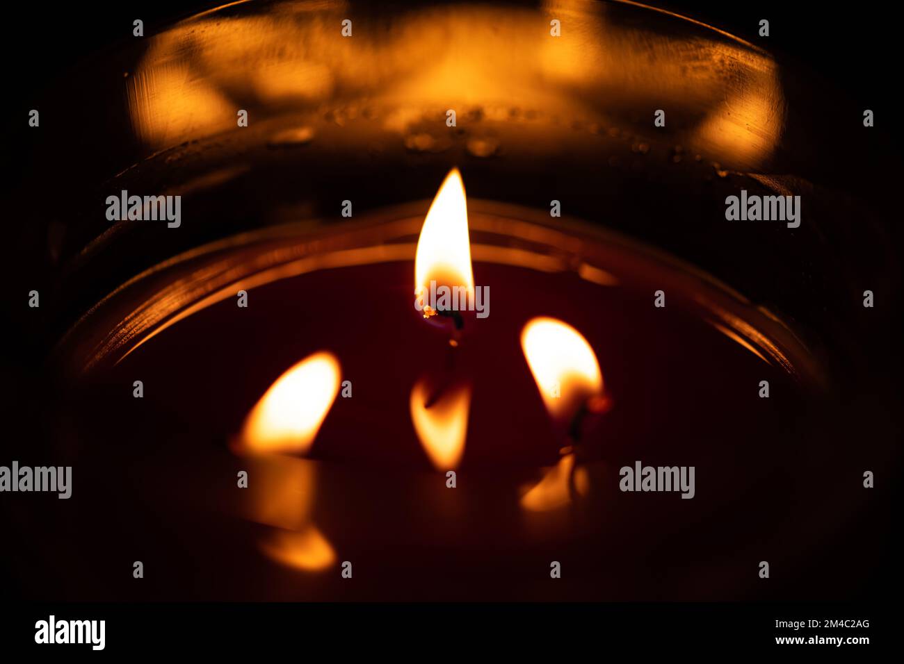 A burning candle with flames and their reflection in the wax, on a dark ...