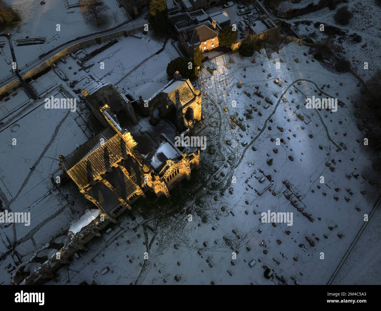 Aerial shot of Melrose Abbey with a layer of snow and frost at sunset ...