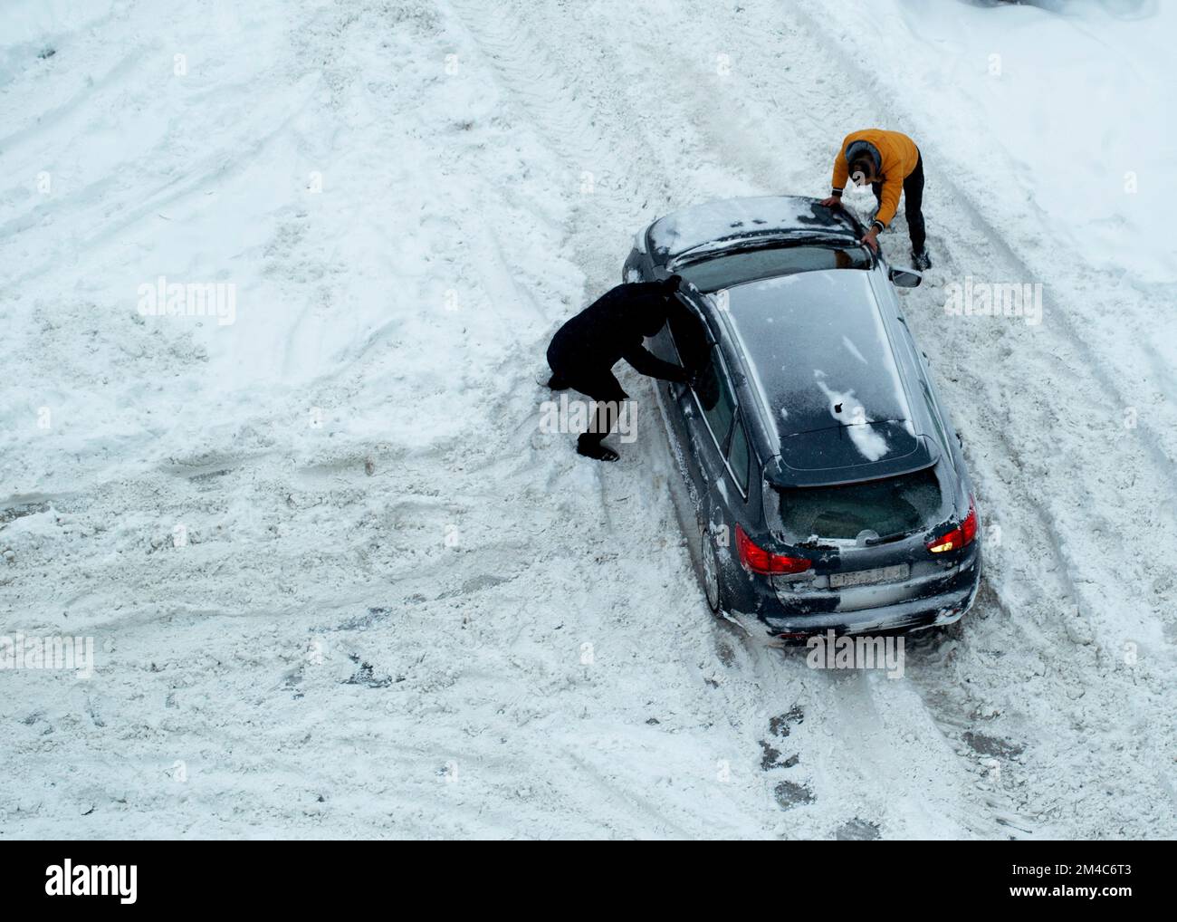 Two men push out a car stuck in the snow. The car skids in a snowdrift ...