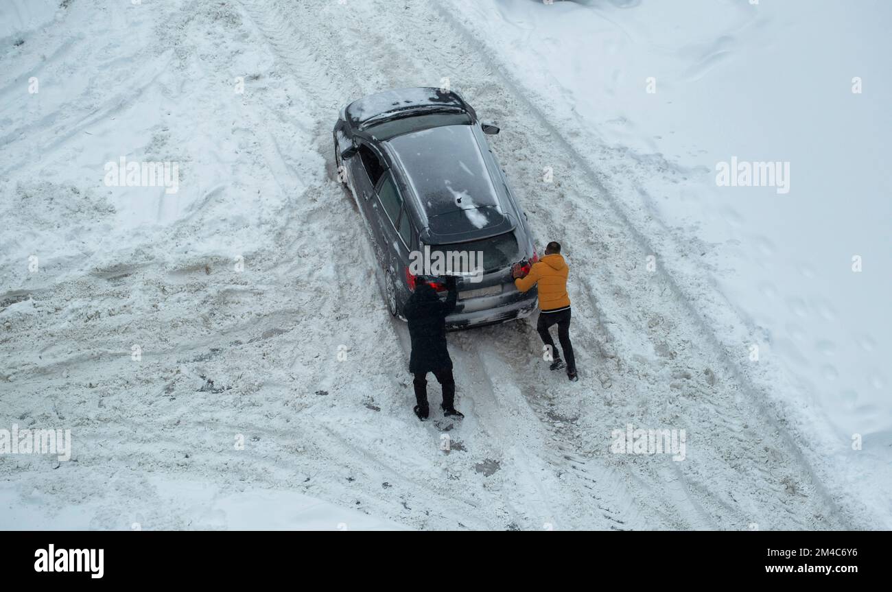 Two men push out a car stuck in the snow. The car skids in a snowdrift ...
