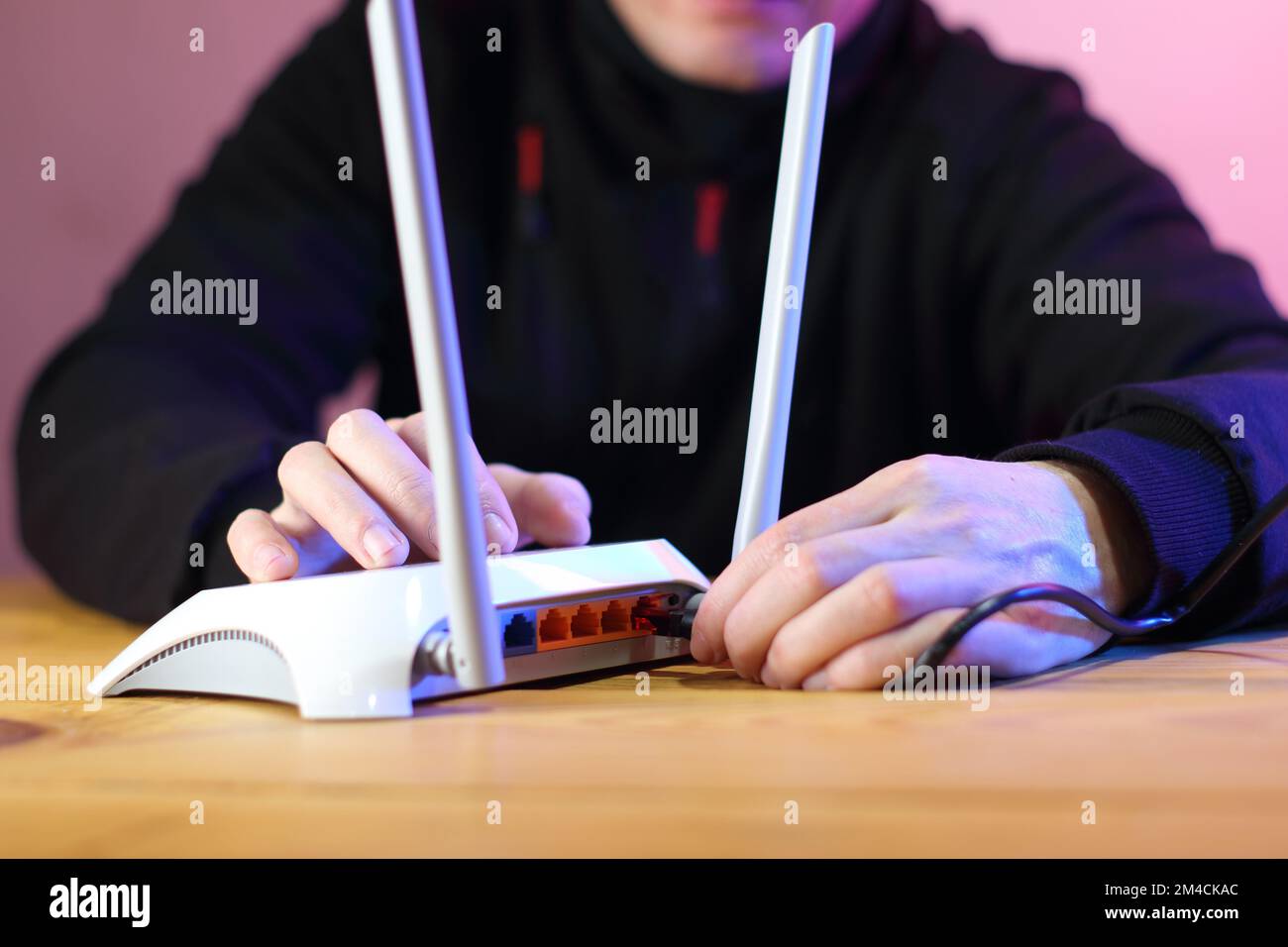 connecting internet cable to router with antennas on table and pink ...