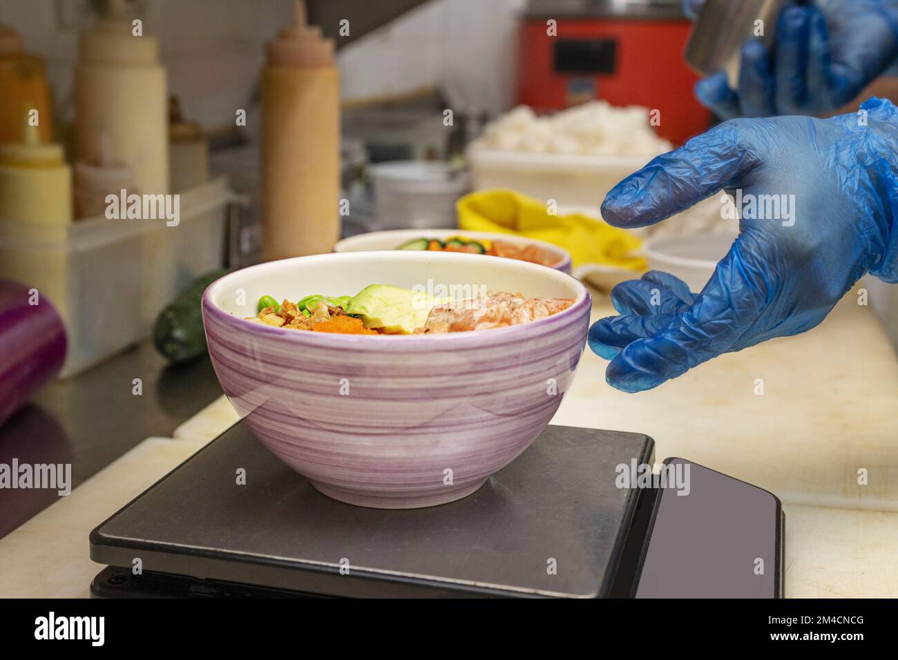 Chef's hands gloved in blue plastic preparing a poke bowl of salmon ...